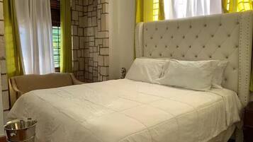 Quarto com uma cama grande, uma cadeira e um balde de metal.