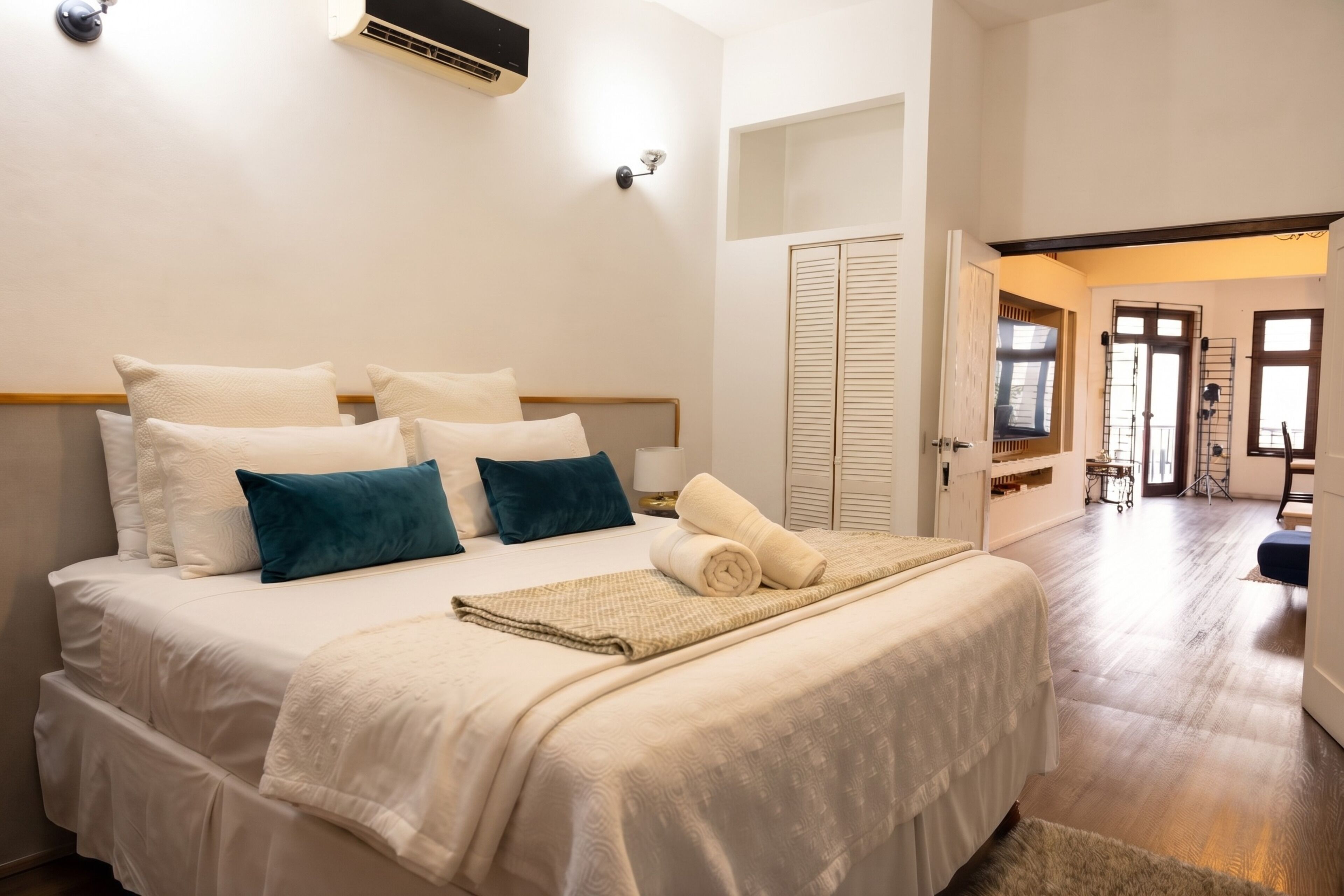 Quarto de hotel com cama grande, mesa de cabeceira, ar condicionado fixado na parede e vista para o corredor.
