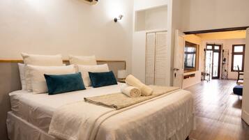 Quarto de hotel com cama grande, mesa de cabeceira, ar condicionado fixado na parede e vista para o corredor.