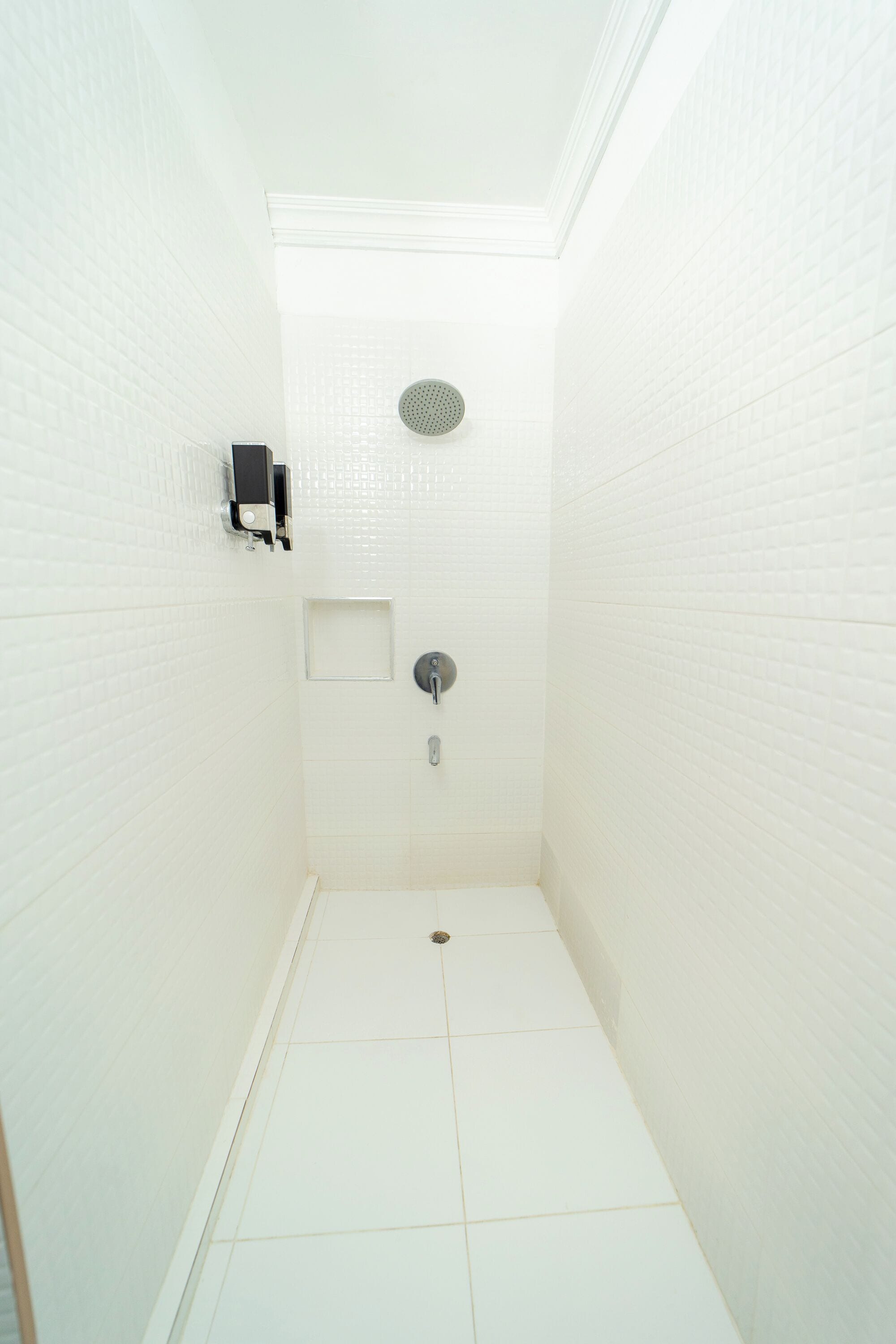 Um pequeno banheiro com azulejos brancos, chuveiro manual e torneira na parede.