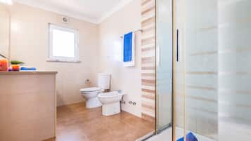 Uma casa de banho moderna com chuveiro, sanita, bidé e janela.