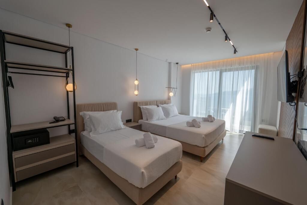 Quarto de hotel com duas camas, uma escrivaninha, televisão e estante.