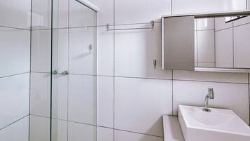 Casa de banho com cabine de duche em vidro, lavatório com espelho e paredes em azulejo.