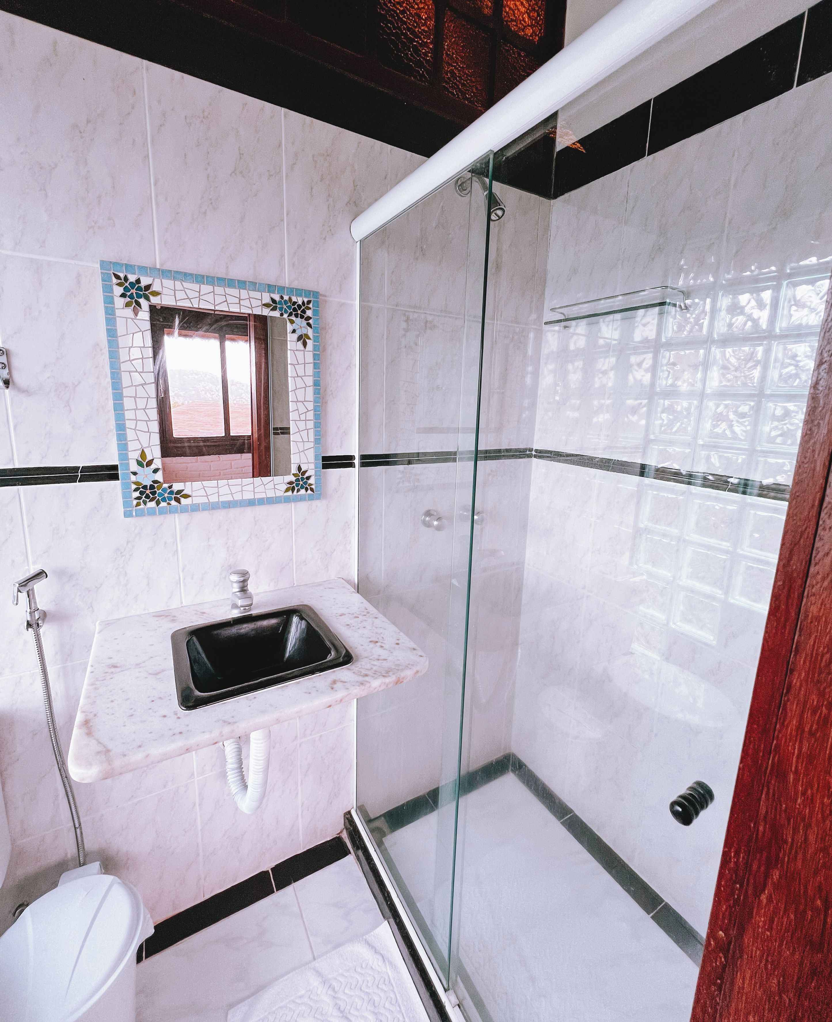 Casa de banho com cabine de duche de vidro, lavatório com espelho e sanita.