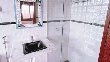 Casa de banho com cabine de duche de vidro, lavatório com espelho e sanita.
