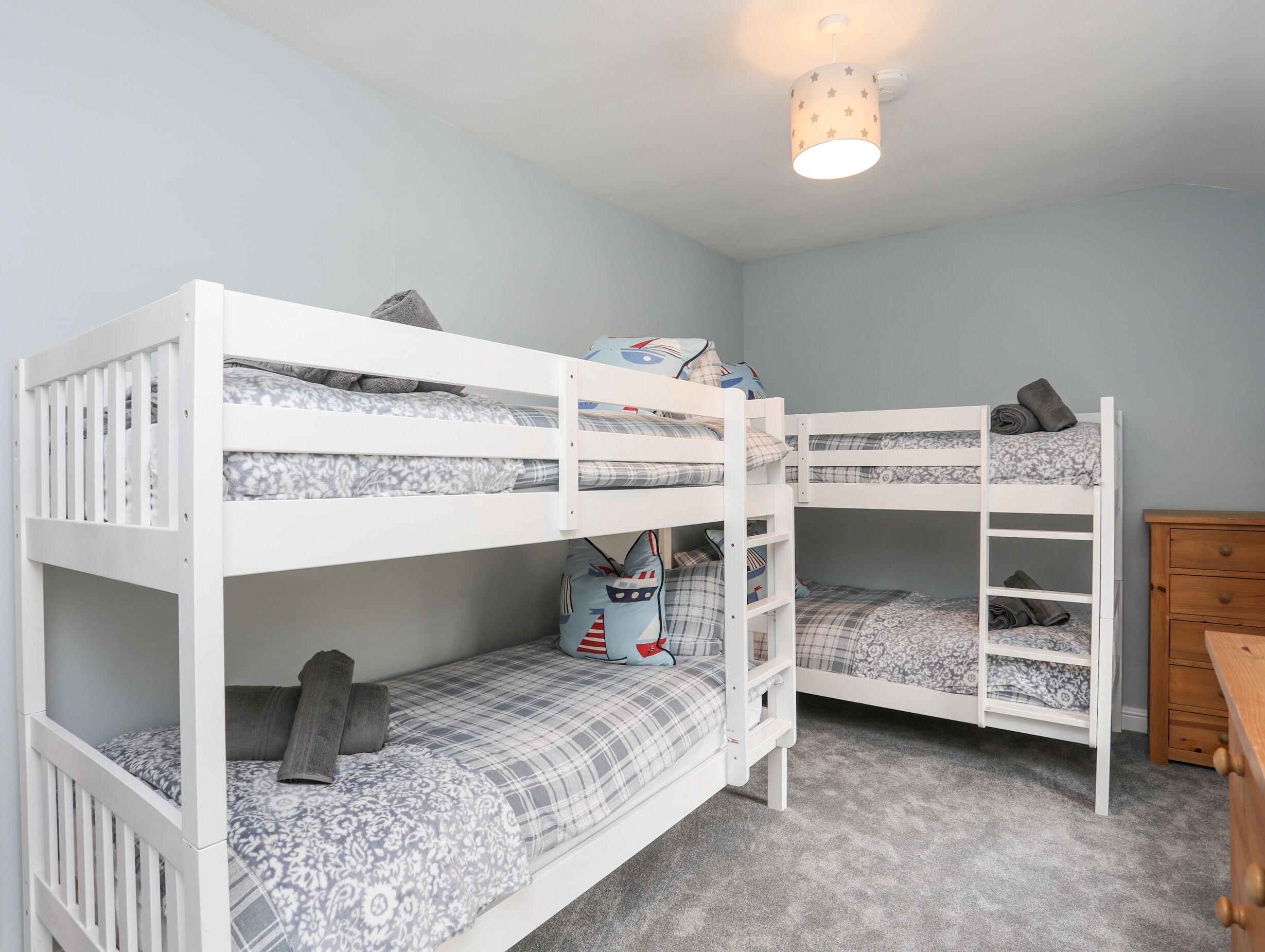 Quarto com beliche, luminária no teto, cómoda de madeira e chão coberto por carpete.
