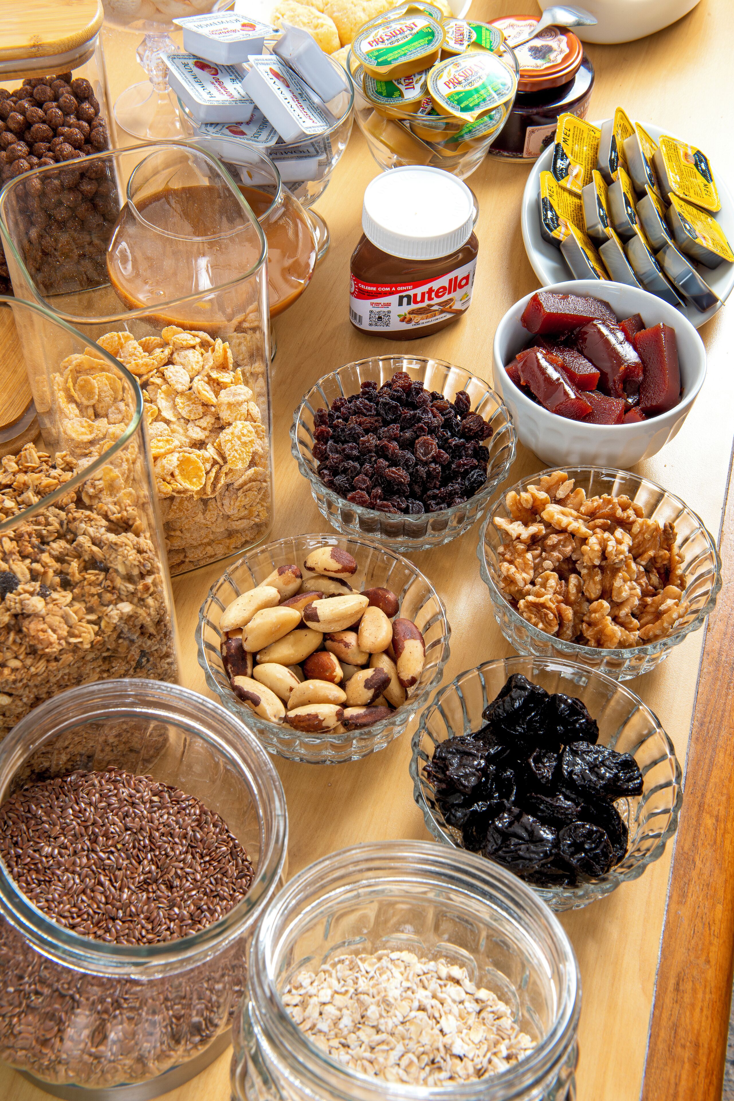 Diversos alimentos como frutos secos, fruta desidratada e granola dispostos sobre uma mesa.