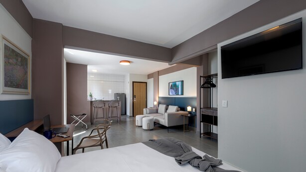 Quarto de hotel moderno com uma cama grande, uma escrivaninha, uma cadeira, um sofá e uma televisão.