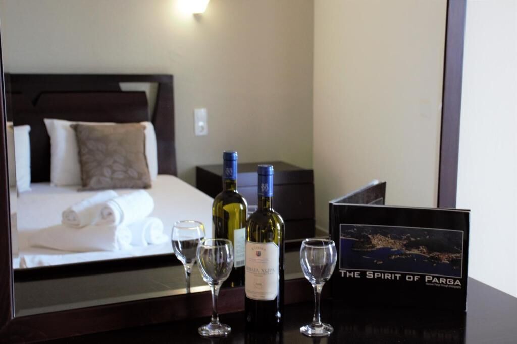 Quarto de hotel com uma cama bem arrumada, duas garrafas de vinho e dois copos sobre uma mesa.