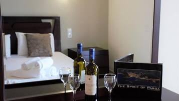 Quarto de hotel com uma cama bem arrumada, duas garrafas de vinho e dois copos sobre uma mesa.