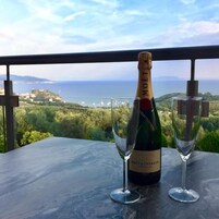 Uma garrafa de champanhe Moët & Chandon sobre uma mesa, com duas taças, com vista para uma paisagem costeira deslumbrante.