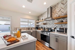 Uma cozinha moderna com armários cinza, uma ilha central, micro-ondas, fogão e painel de backsplash em padrão herringbone.