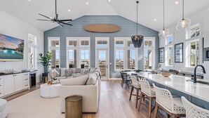 Uma sala de estar espaçosa com um sofá grande, uma área de jantar com banquetas altas e uma cozinha com ilha central.