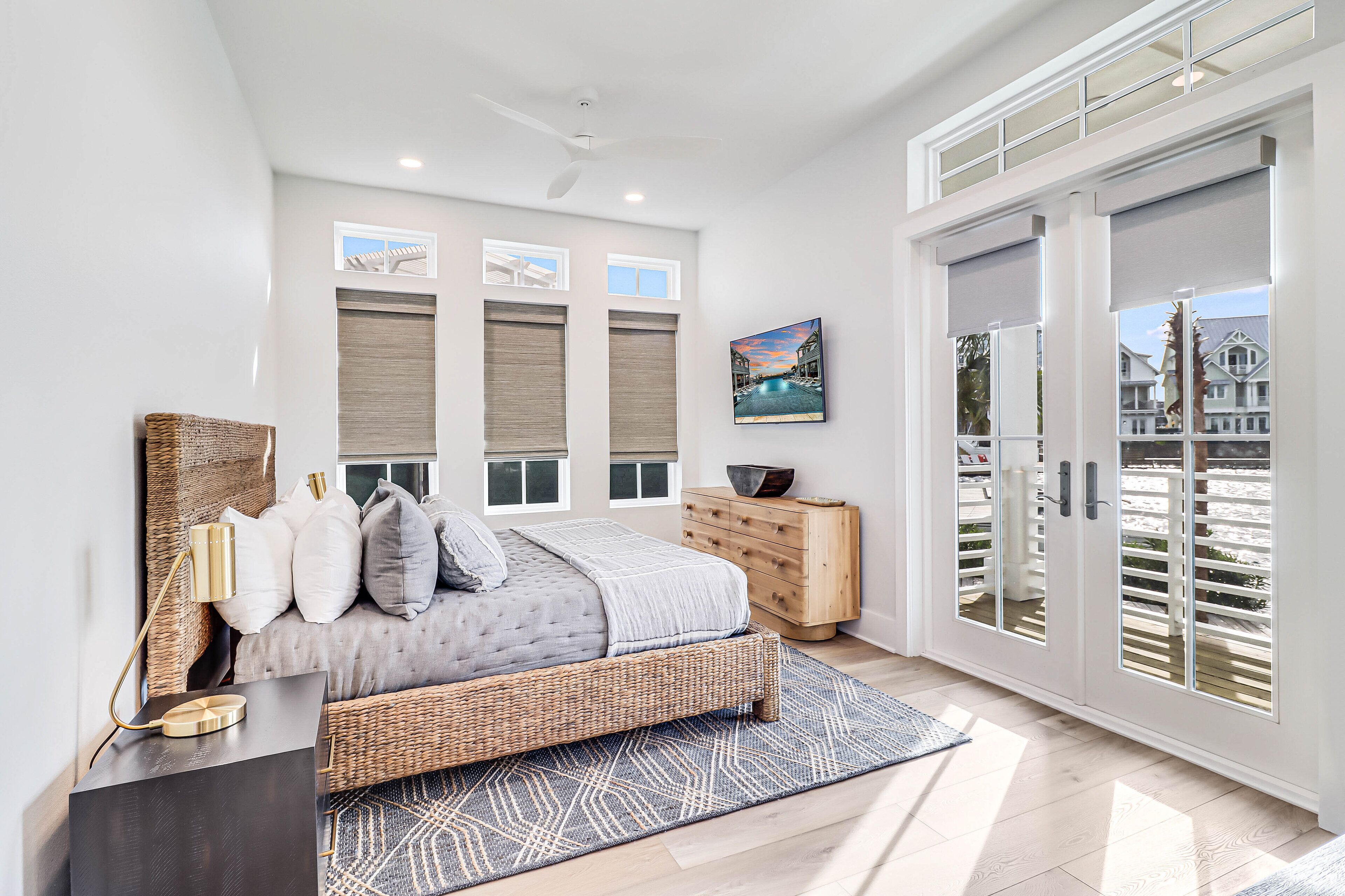 Quarto moderno com uma cama grande, mesa de cabeceira, cômoda e vista para o exterior por uma porta de vidro deslizante.