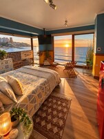 Quarto com cama grande, vista para o mar, varanda e paisagem urbana.
