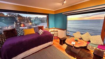 Quarto moderno com uma cama grande, um sofá pequeno, uma mesa de centro e vista para a cidade e oceano.