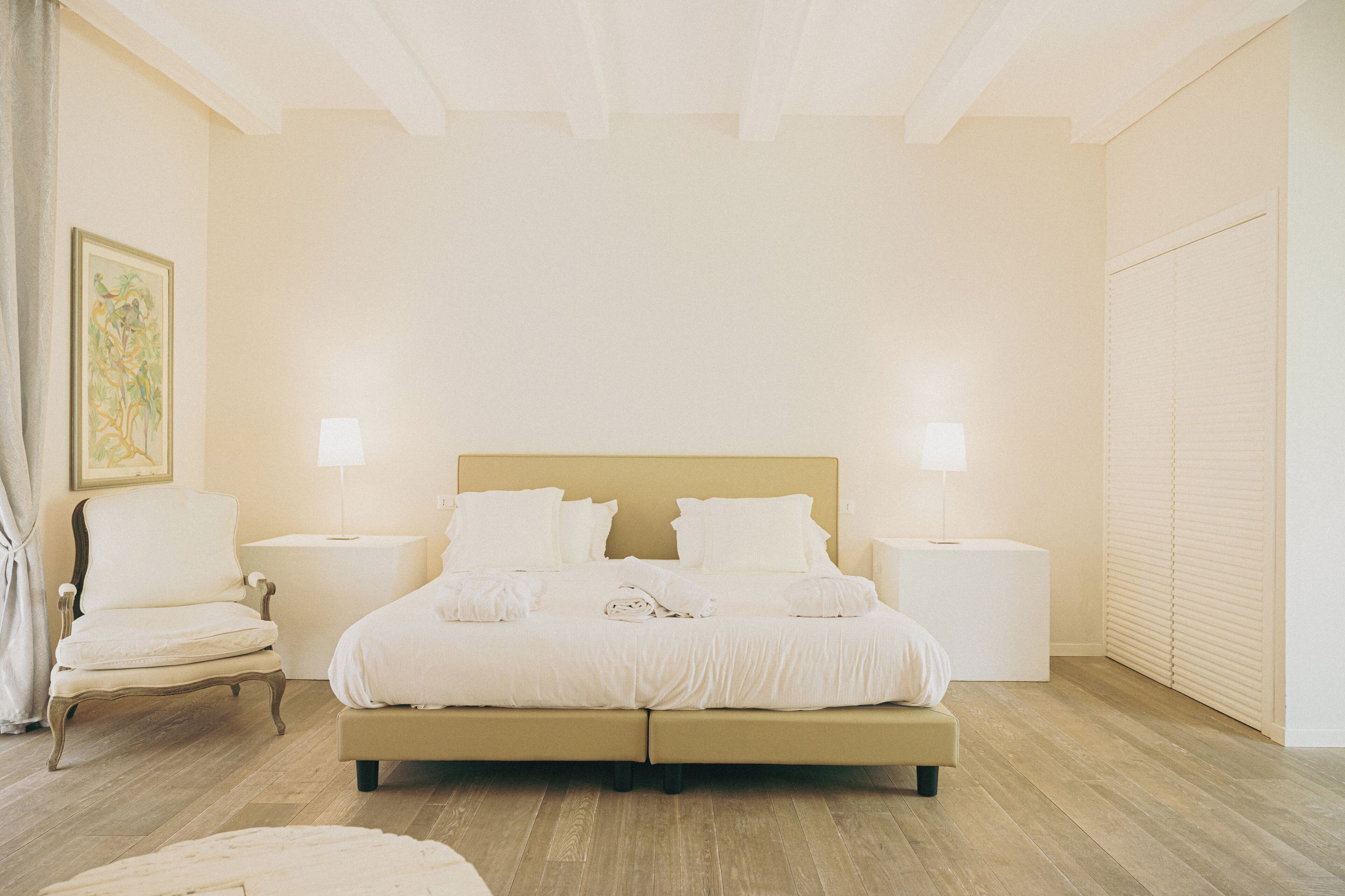 Quarto bem organizado com uma cama grande, duas mesas de cabeceira, uma cadeira e um quadro na parede.