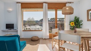 Uma sala de estar moderna com televisão, sofá, mesa de jantar e vista para o exterior.