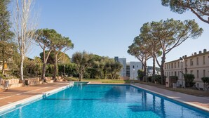 Piscina retangular com água azul cristalina, rodeada por árvores e um calçadão pavimentado.