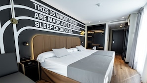 Quarto de hotel moderno com uma cama grande, mesas de cabeceira, um guarda-roupa e uma frase motivacional na parede.