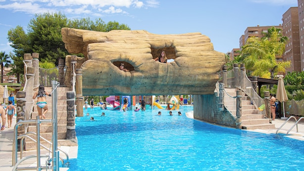 Uma área de piscina com uma estrutura rochosa, escadas para entrar na piscina e um escorregador.