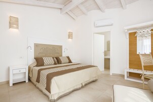 Quarto com cama, mesas de cabeceira, guarda-roupa e um banquinho.