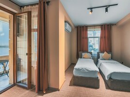 Quarto de hotel com duas camas, uma porta de correr de vidro e uma varanda.