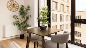 Uma sala de estar moderna com uma mesa de madeira, duas cadeiras, uma janela grande e duas plantas de bambu em vasos.