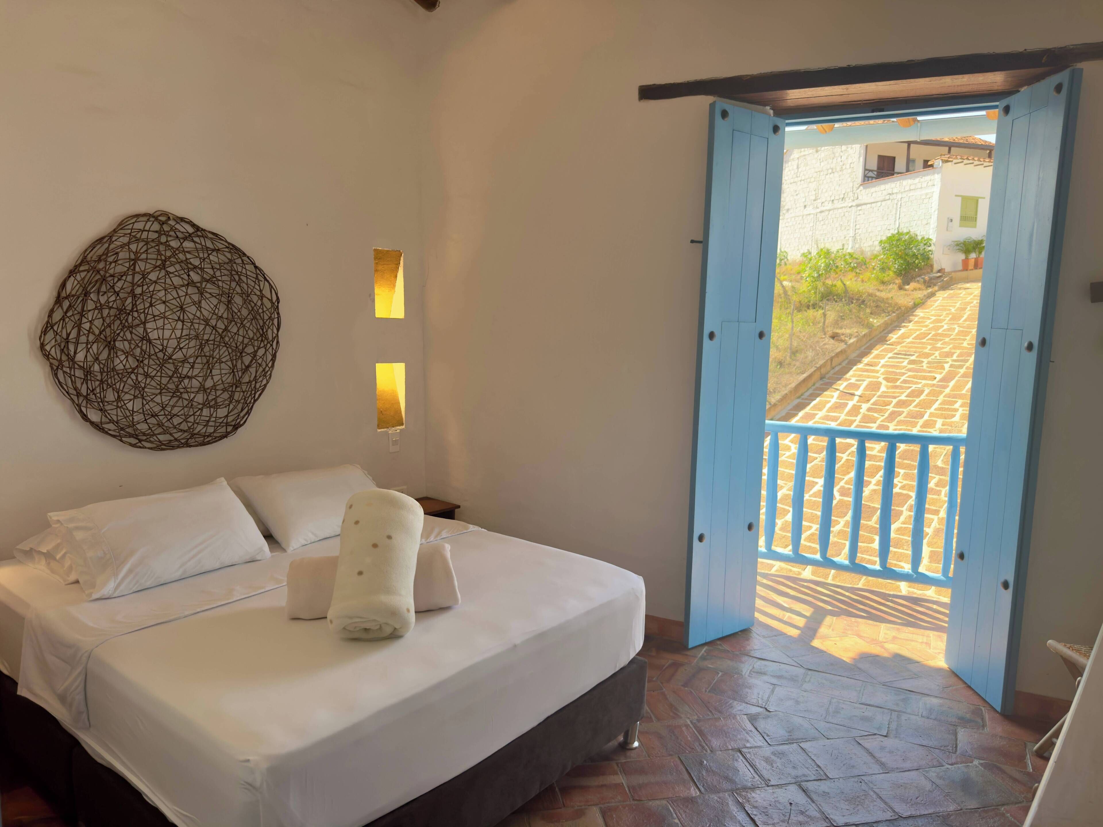 Quarto com cama, luminária na parede e porta aberta para um pátio.