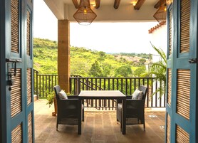 Varanda com mesa e duas cadeiras, vista para uma paisagem verdejante com casas ao longe.