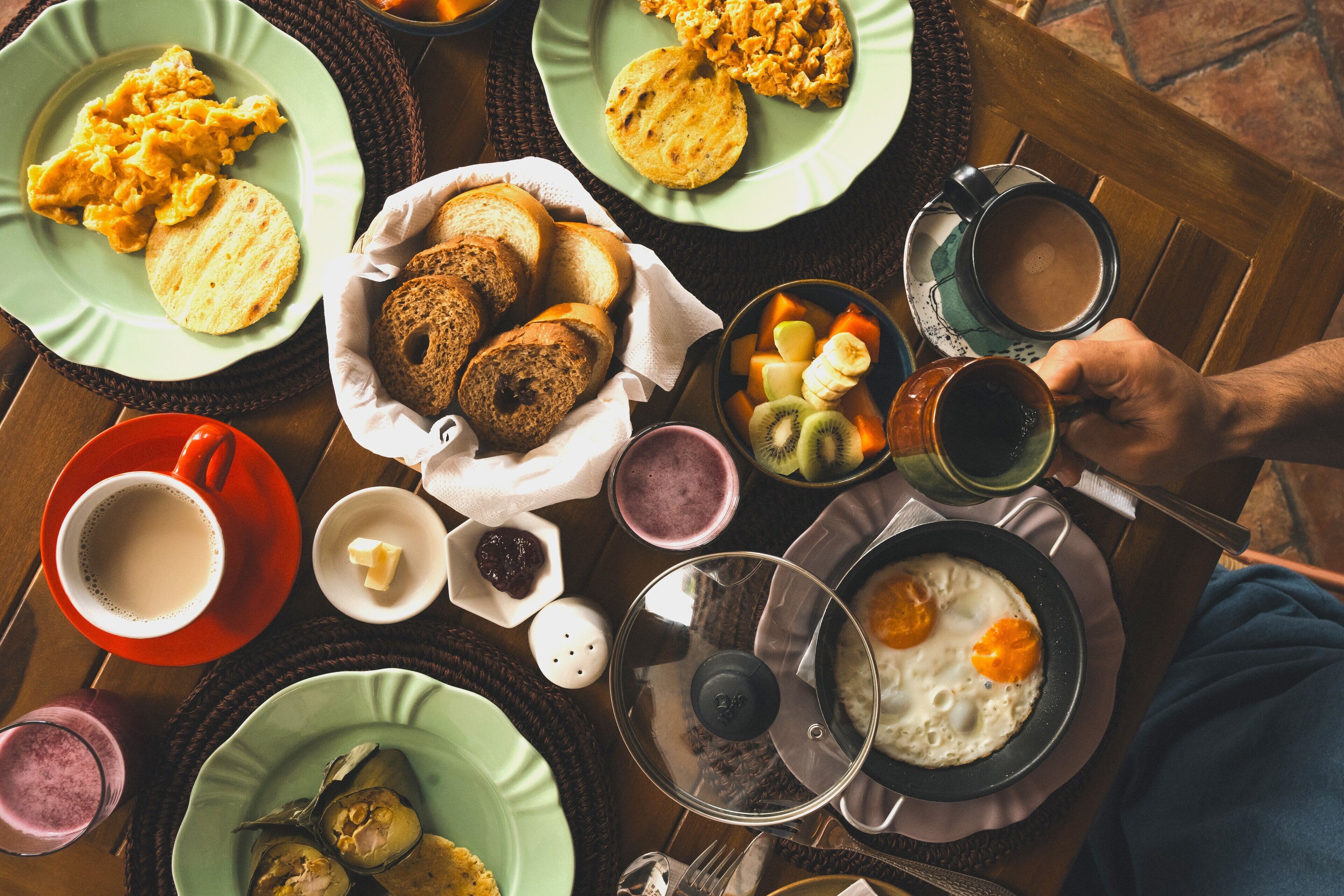 Uma mesa com diversos itens de pequeno-almoço, incluindo ovos mexidos, torradas e fruta.