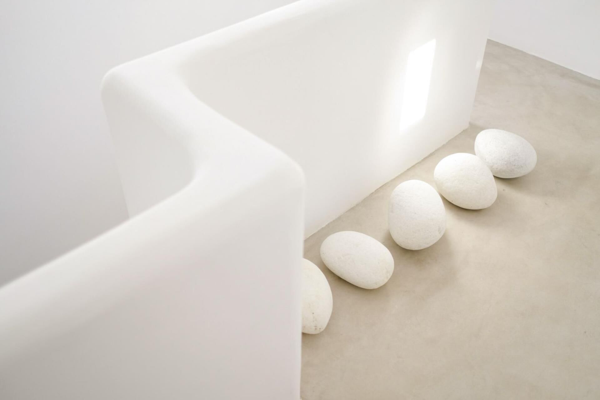 Um interior moderno e minimalista, com uma estrutura branca curva e uma série de pedras brancas sobre um chão bege.