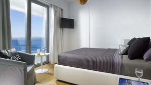 Quarto de hotel moderno com uma cama grande, uma mesinha com um copo, um sofá com um almofada e uma televisão na parede.