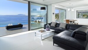 Sala de estar moderna com uma grande porta de vidro que dá para uma varanda com vista para o mar.