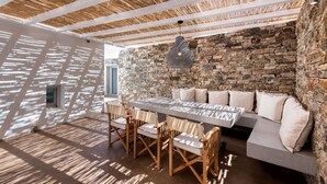 Um interior moderno com parede de pedra, vigas de madeira no teto e uma área de jantar com uma mesa comprida e cadeiras.