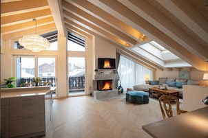 Uma sala de estar ampla com lareira, vigas de madeira, um sofá e uma mesa de jantar.