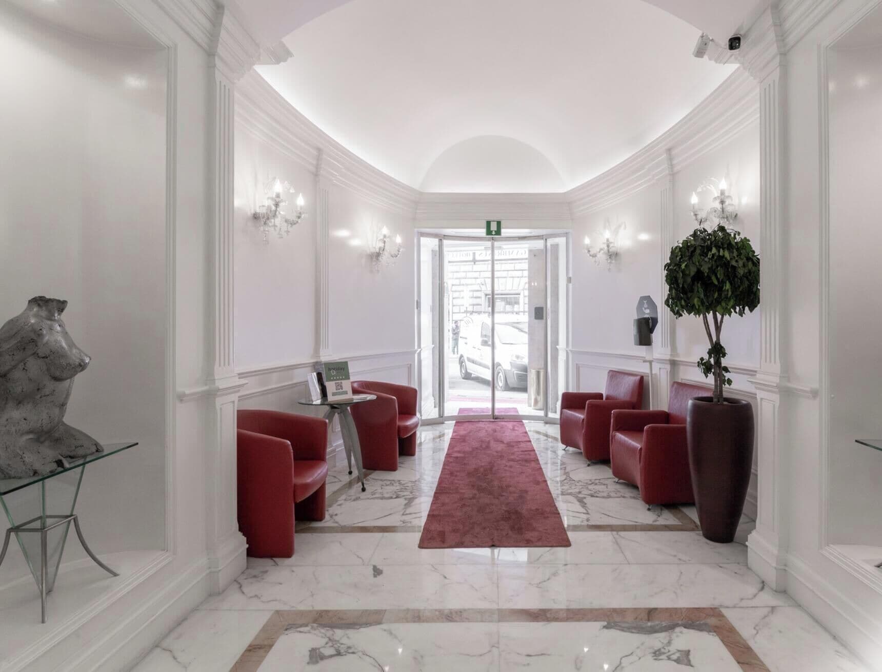 Um hall de hotel com piso de mármore, assentos vermelhos, um lustre e uma estátua.