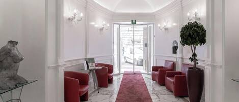 Um hall de hotel com piso de mármore, assentos vermelhos, um lustre e uma estátua.