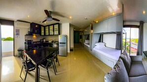 Quarto de hotel moderno com cozinha compacta, sofá, TV e varanda com vista.
