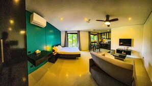 Quarto de hotel moderno com uma cama, escrivaninha, cadeira, televisão e ventoinha no teto.
