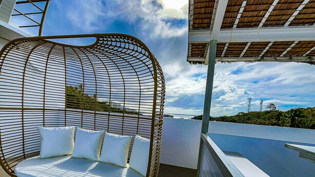 Uma área de estar moderna ao ar livre, com uma cadeira trançada única e vista para o mar.