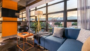 Uma sala de estar moderna com uma janela grande, um sofá, uma escrivaninha e uma luminária.
