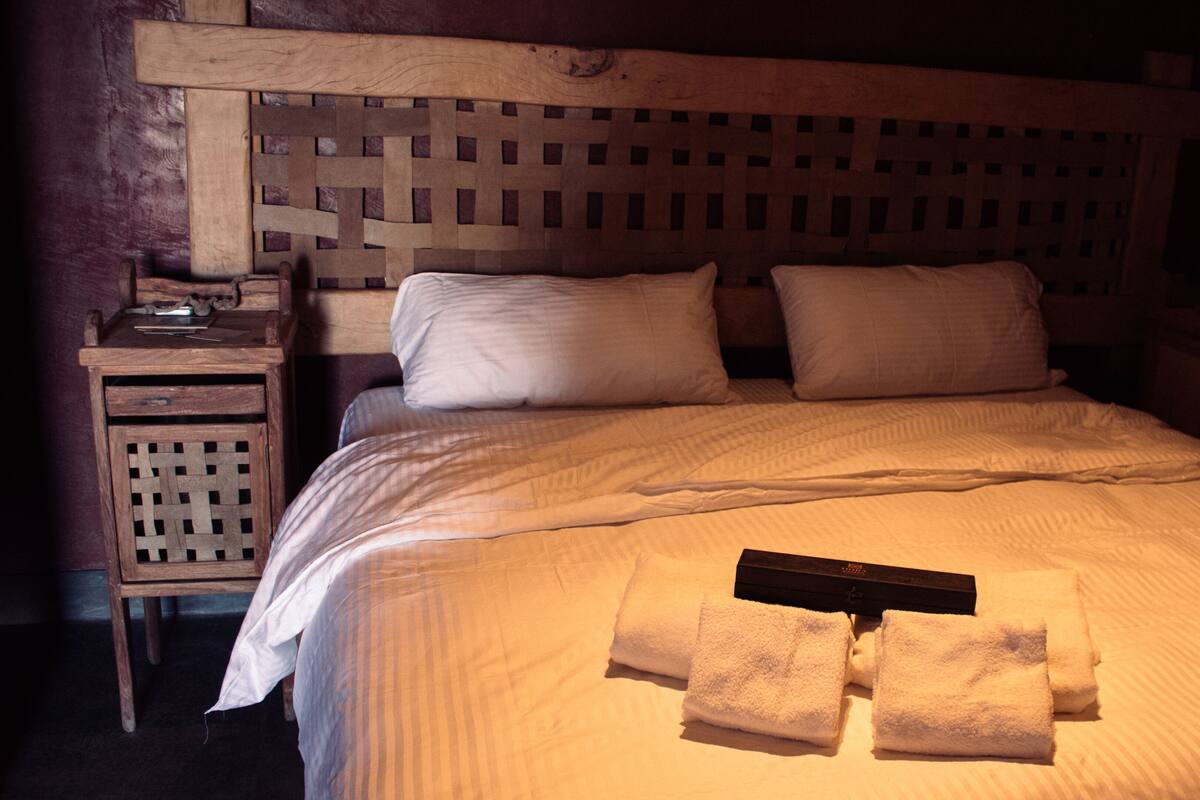Uma cama com cabeceira de madeira, roupa de cama branca e duas toalhas sobre a cama.