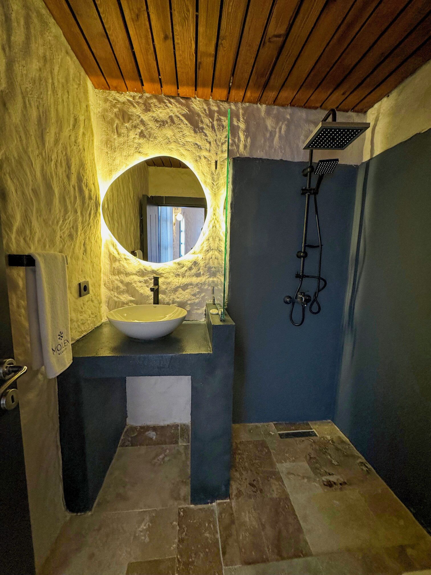 Casa de banho com lavatório de pedra, espelho redondo e chuveiro.