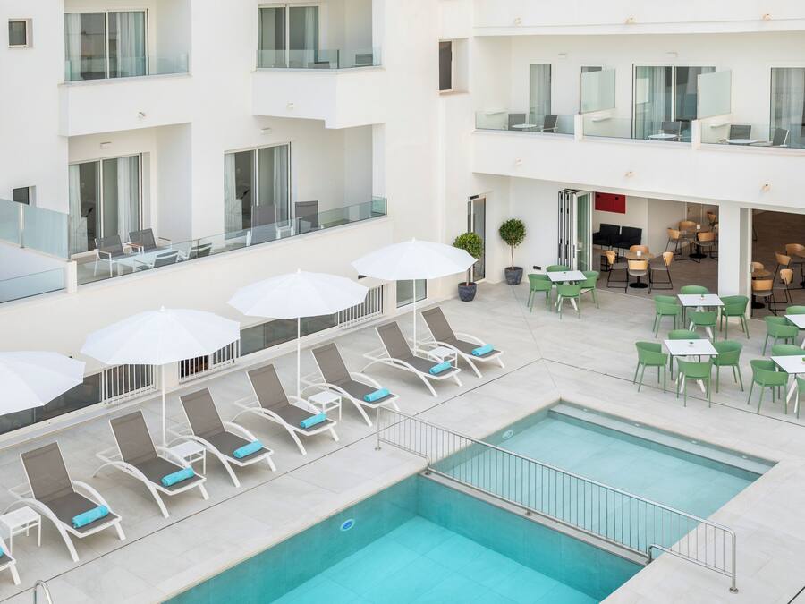 Área de piscina de hotel com espreguiçadeiras, guarda-sóis e um espaço de refeições com mesas e cadeiras.