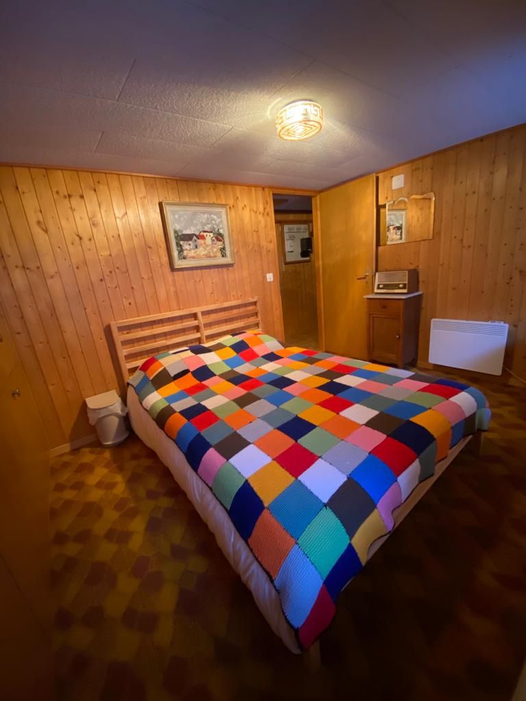 Um quarto com piso de madeira, cama com colcha colorida, mesa de cabeceira, cômoda e espelho.