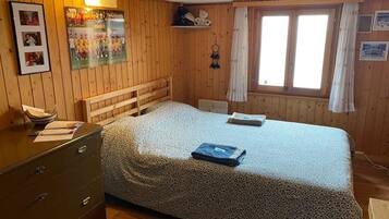 Um quarto com paredes de madeira, uma cama, uma cômoda, um cartaz e uma janela com cortinas.