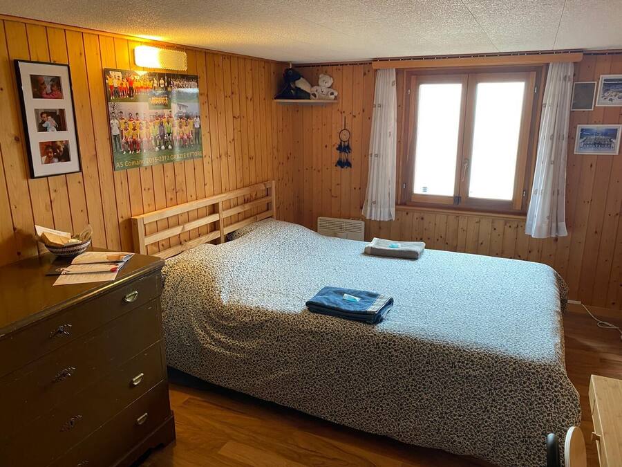 Um quarto com paredes de madeira, uma cama, uma cômoda, um cartaz e uma janela com cortinas.