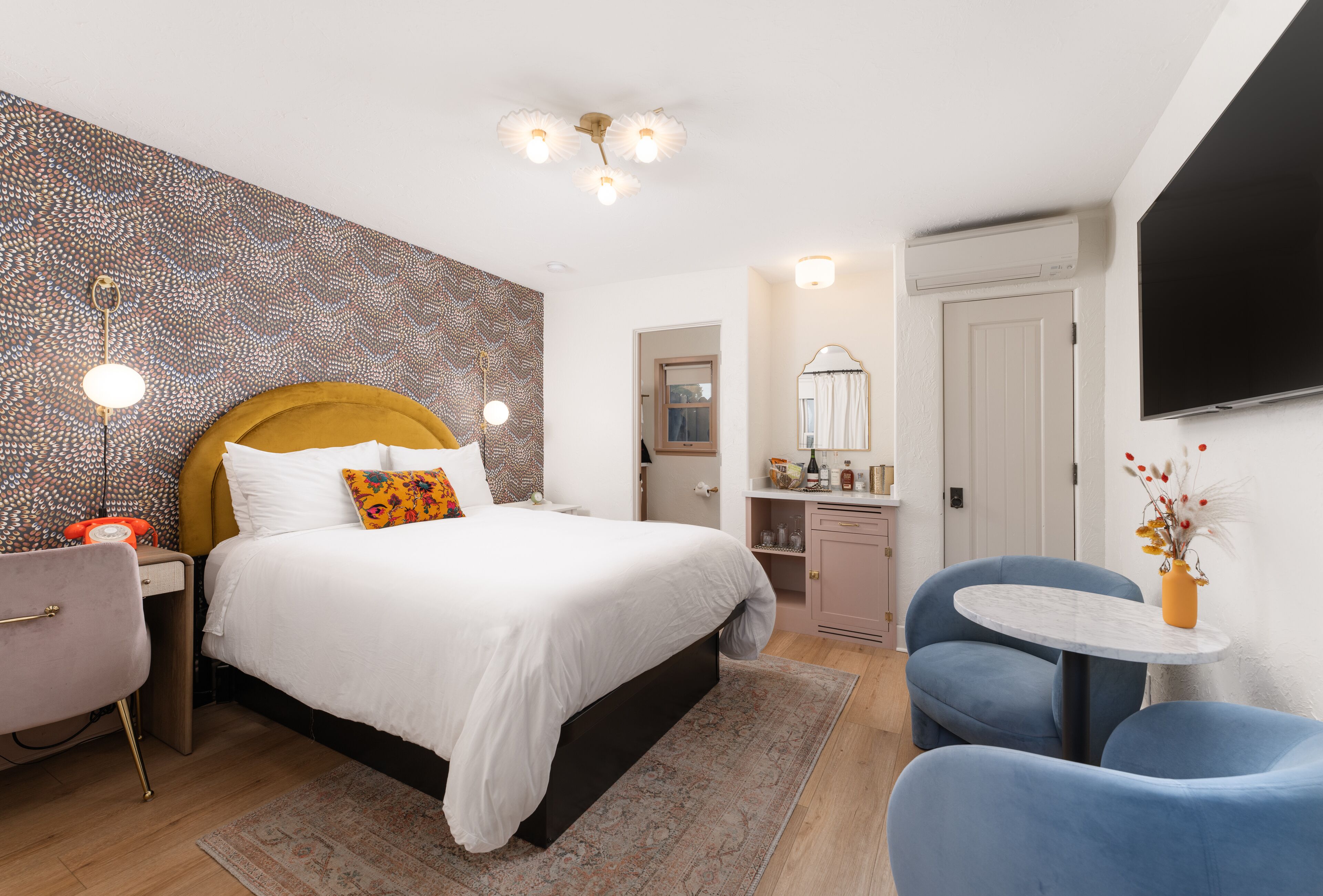 Quarto de hotel moderno com uma cama grande, uma escrivaninha, uma cadeira, uma mesa pequena e uma televisão.