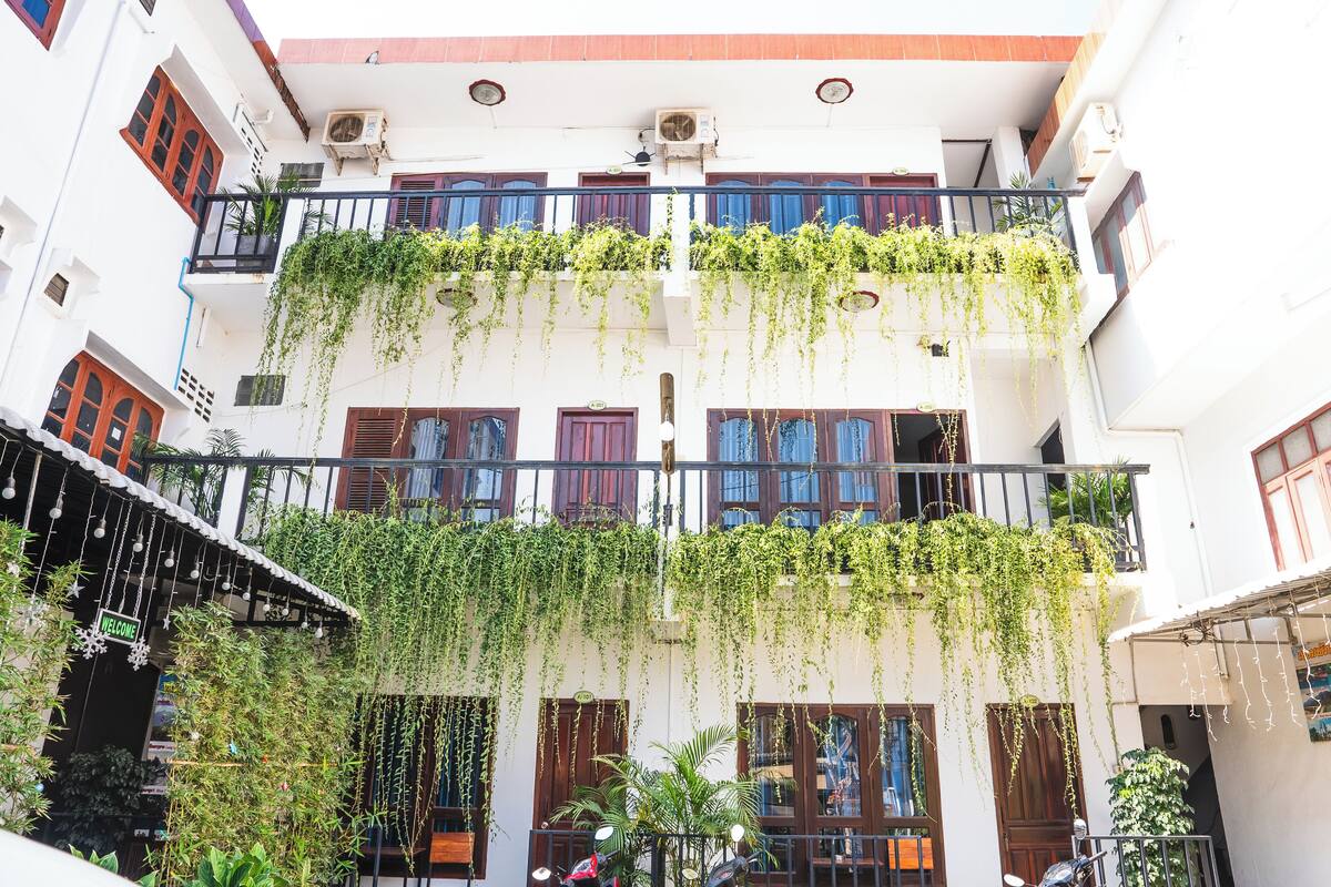 Um edifício com vários andares, varandas cobertas de vegetação, uma placa de boas-vindas e uma entrada visível.